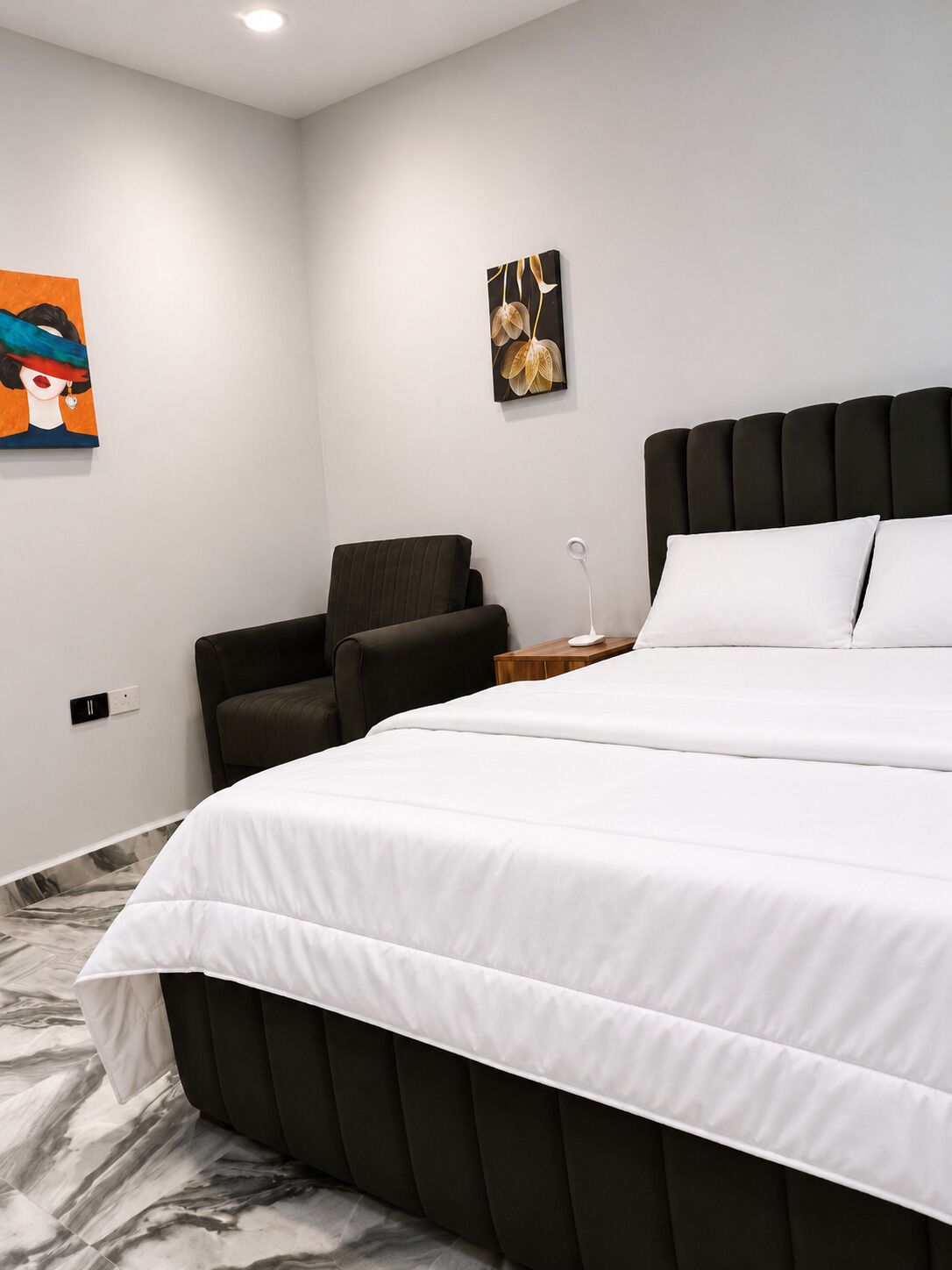 Quarto moderno com uma cama grande, uma cadeira e duas obras de arte nas paredes.