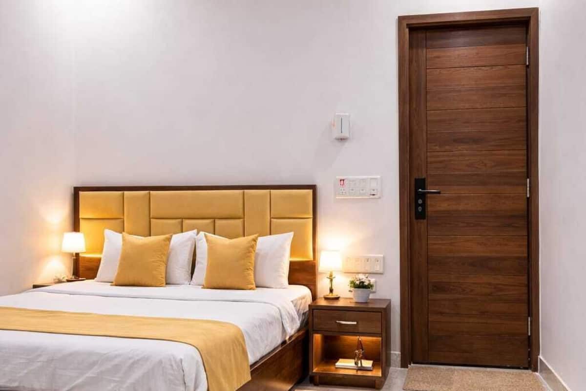 Quarto de hotel com cama de madeira, piso de mármore, mesa de cabeceira com abajur e porta de madeira.