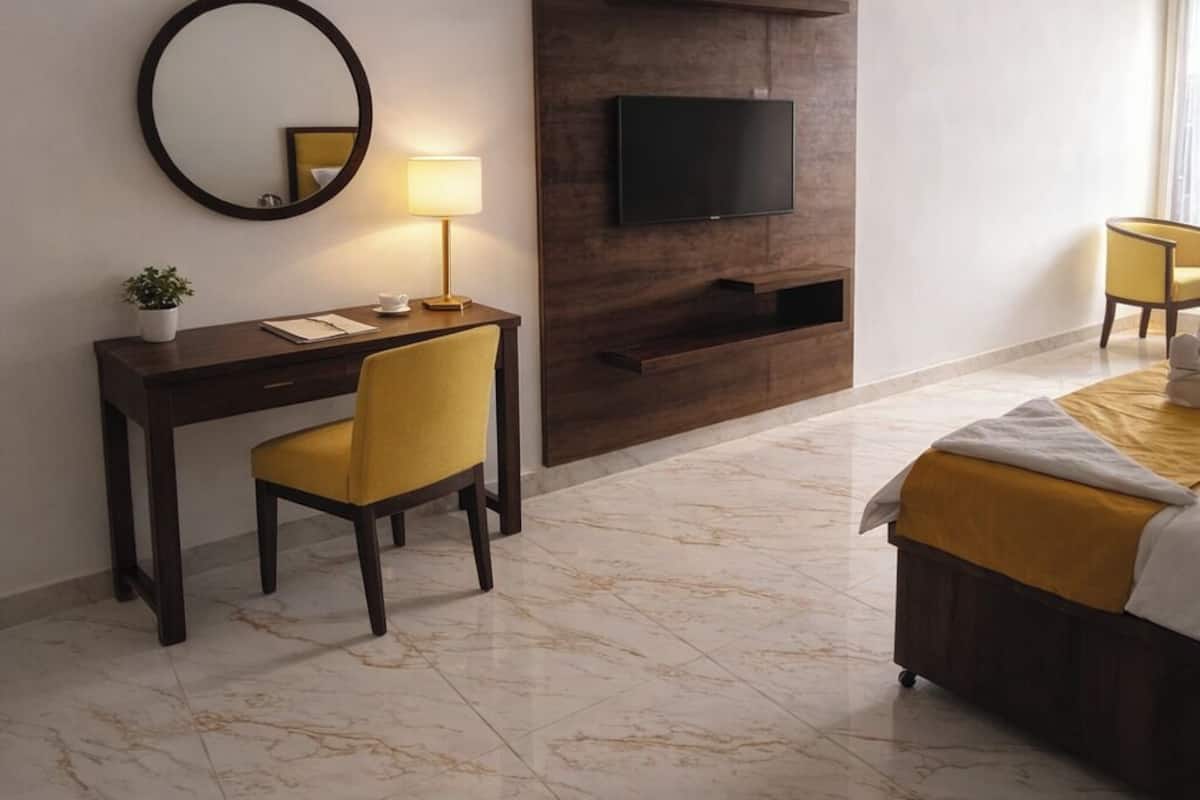 Quarto de hotel com cama, escrivaninha com cadeira, televisão presa a um painel de madeira, espelho redondo e uma pequena planta em vaso.