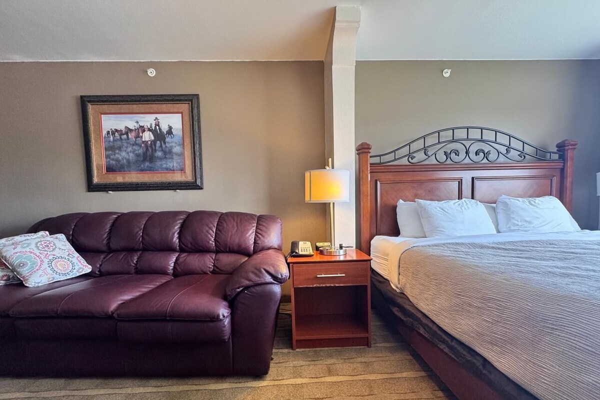 Quarto de hotel com sofá de couro, mesa de cabeceira com abajur e cama com roupa de cama branca.