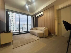 Uma sala de estar moderna com um sofá, uma TV de tela plana, uma janela grande com vista para a cidade e um aparelho de ar condicionado.