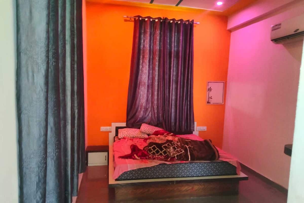 Um quarto pequeno e colorido com uma cama, uma cortina e um ar condicionado fixado na parede.