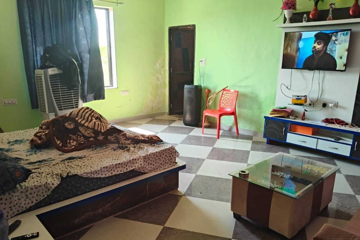 Quarto com uma cama, televisão, uma cadeira vermelha e uma mesinha com tampo de vidro.