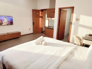 Quarto de hotel com cama, televisão, guarda-roupa de madeira, escrivaninha e uma cadeira.