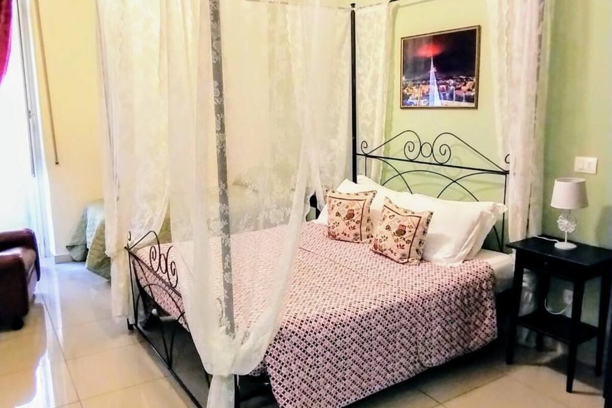 Quarto com cama de dossel, mesa de cabeceira, luminária e pintura com vista urbana na parede.