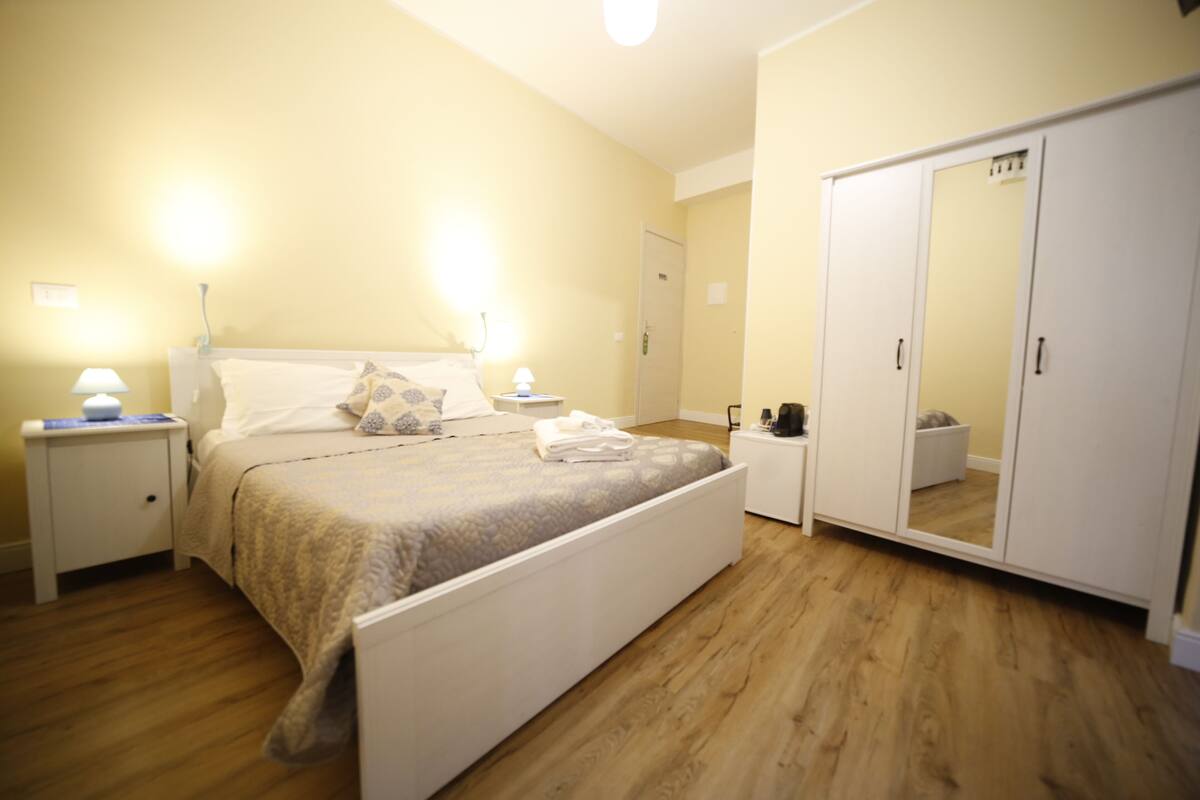 Quarto com cama, mesas de cabeceira, guarda-roupa e espelho.