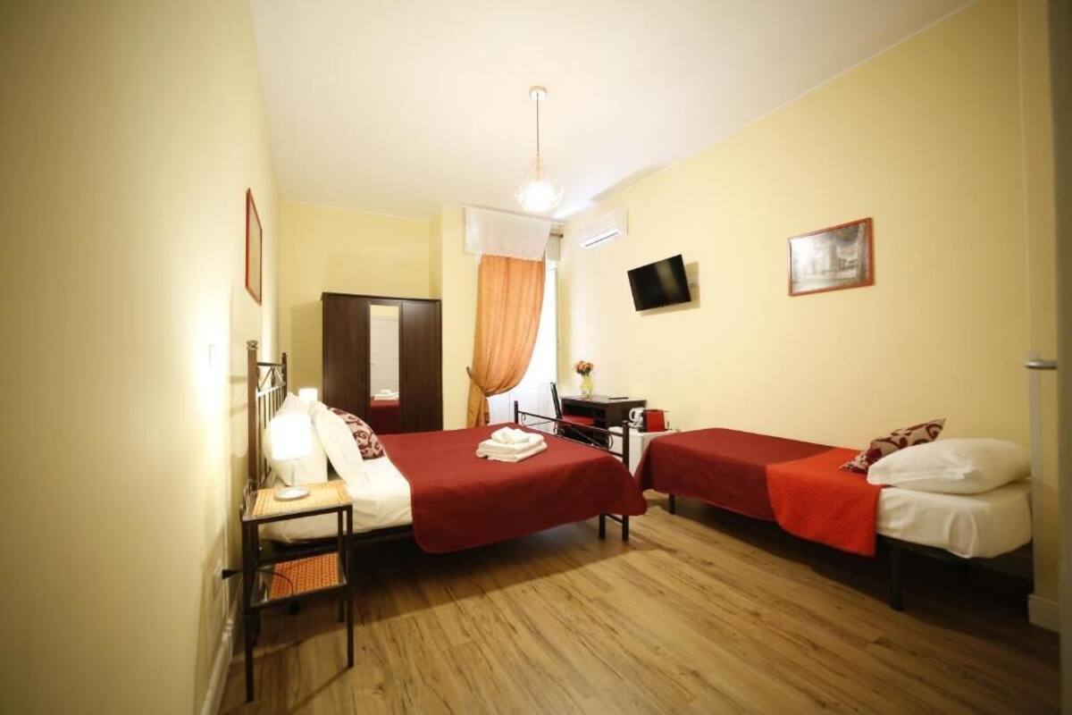 Quarto de hotel com duas camas, uma escrivaninha, uma cadeira, uma televisão e uma porta.