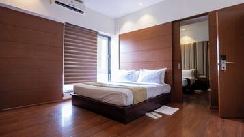 Quarto moderno com piso de madeira, uma cama grande com roupa de cama branca, uma porta deslizante para um banheiro e um aparelho de ar condicionado na parede.