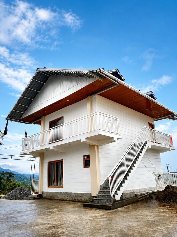 Uma casa de dois andares com varanda, escada e vista para as montanhas.