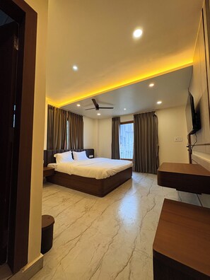 Quarto de hotel moderno com uma cama grande, ventilador de teto e televisão fixada na parede.