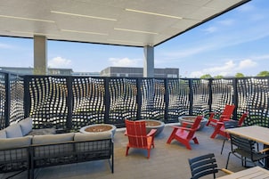 Uma área externa com assentos em design moderno, combinando móveis vermelhos e cinzas, um cercado decorativo com detalhes circulares e uma vista desimpedida do céu.