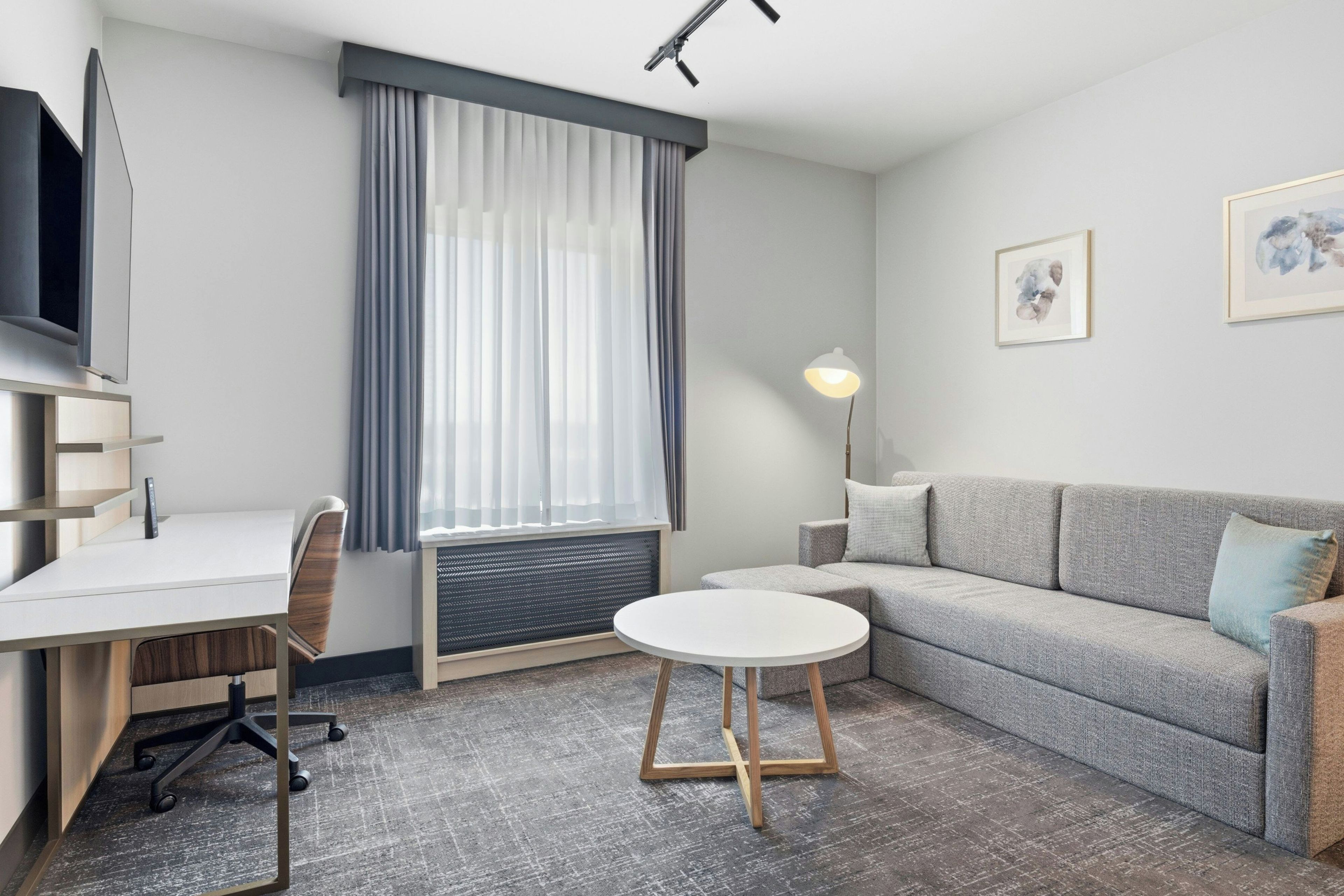 Quarto de hotel moderno com escrivaninha, cadeira, sofá e mesa redonda.