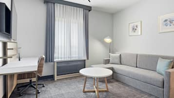 Quarto de hotel moderno com escrivaninha, cadeira, sofá e mesa redonda.