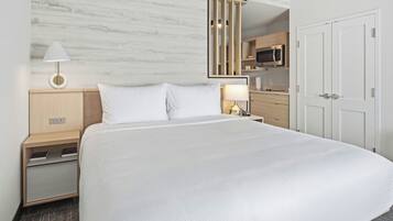 Quarto de hotel com cama, mesas de cabeceira, luminária, armário e micro-ondas.