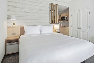 Quarto de hotel com cama, mesas de cabeceira, luminária, armário e micro-ondas.