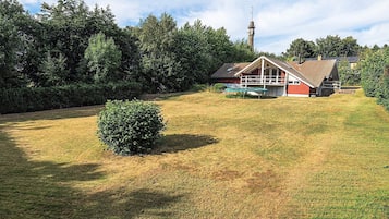 Um imóvel residencial com um gramado amplo, um arbusto pequeno e uma casa com varanda.