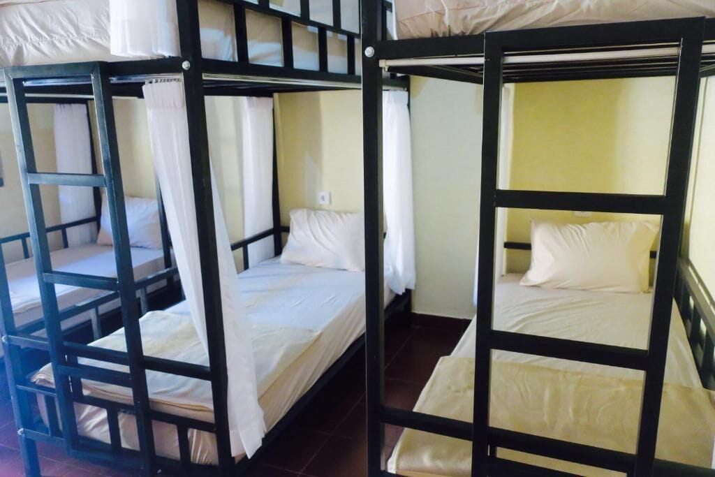 Quarto com beliches, cada um com colchão e travesseiro brancos, e uma escada fixada nos beliches.