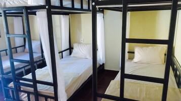 Quarto com beliches, cada um com colchão e travesseiro brancos, e uma escada fixada nos beliches.