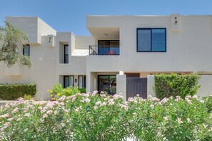 Um edifício moderno de dois andares com varanda, portão e um jardim com plantas floridas.
