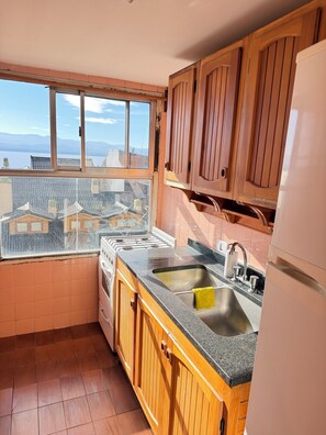Uma cozinha com armários de madeira, fogão, pia e janela com vista para edifícios e montanhas.