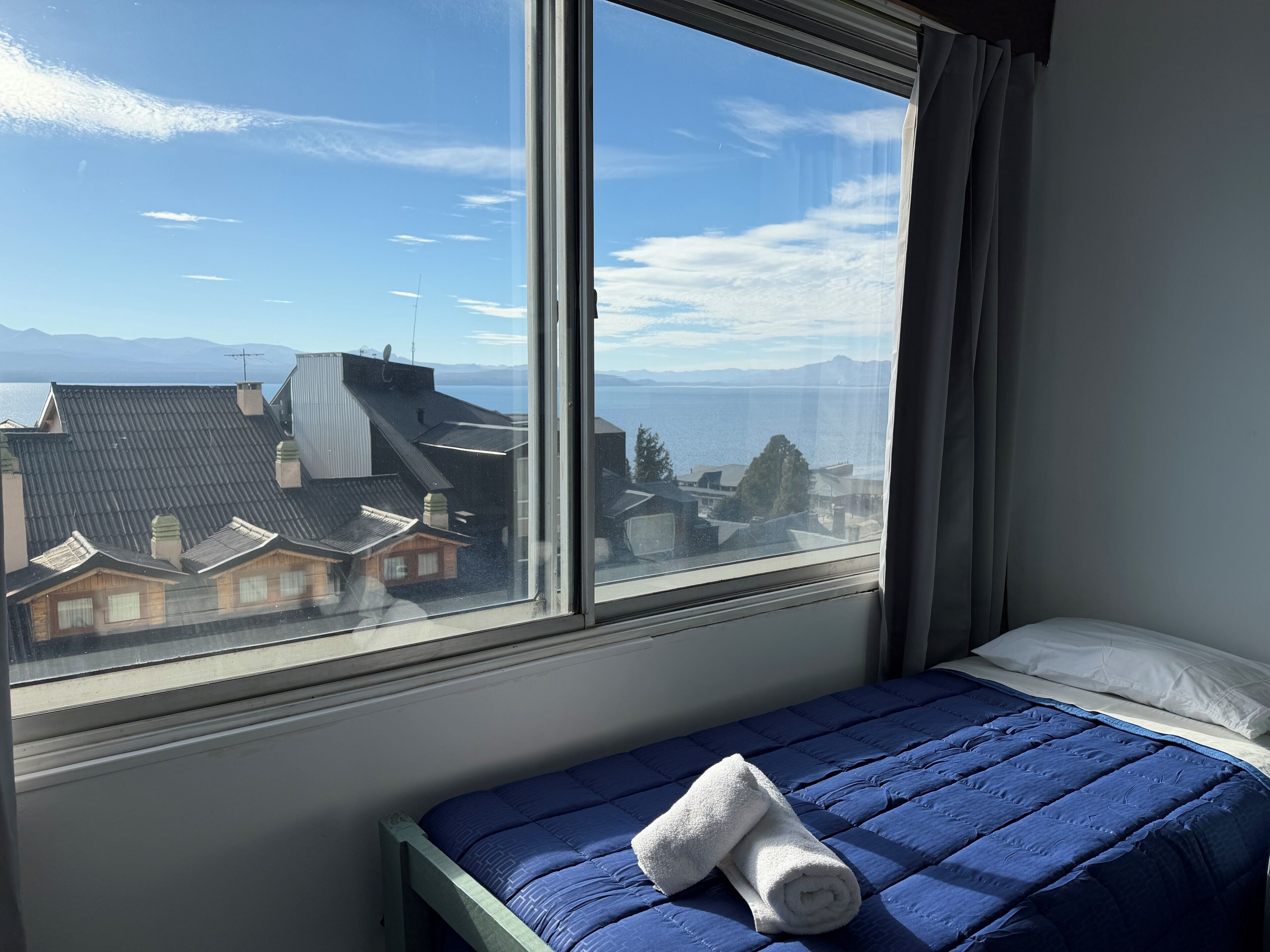 Quarto com cama, janela e vista para edifícios e montanhas.