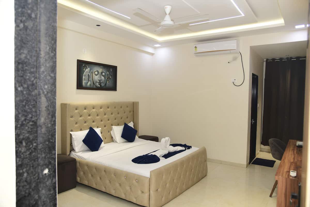 Quarto com cabeceira estofada, cama com roupa de cama branca e azul, mesa de cabeceira, ar condicionado fixado na parede e ventoinha de teto.