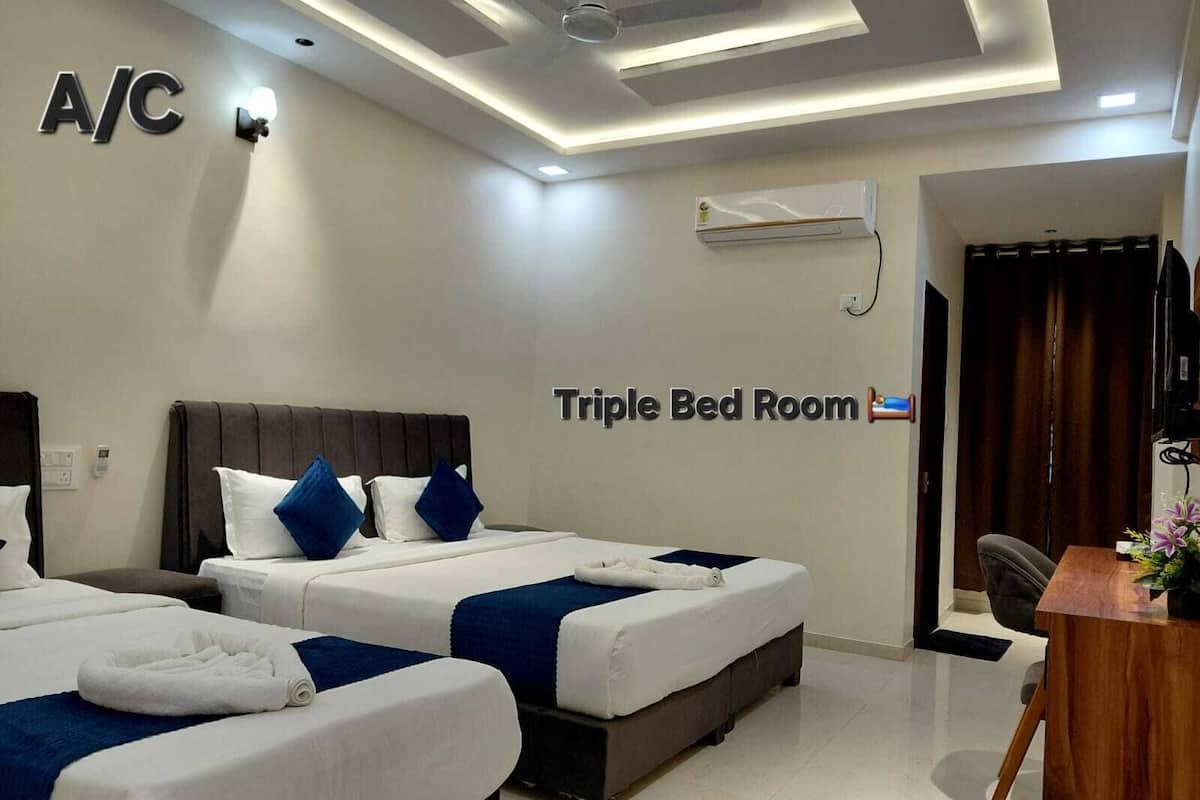 Quarto triplo com três camas, ventilador de teto, ar condicionado e uma mesa com cadeira.