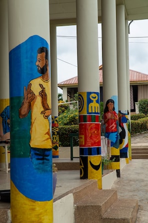 Um edifício com murais coloridos nas colunas e uma pessoa vestindo uma camisa vermelha.