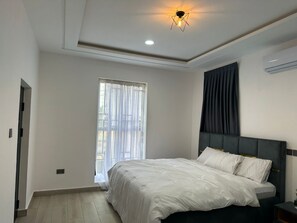 Quarto com cama, janela com cortinas, aparelho de ar condicionado e luminária no teto.