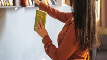 Uma pessoa num quarto com estantes, uma cadeira vermelha e um livro.