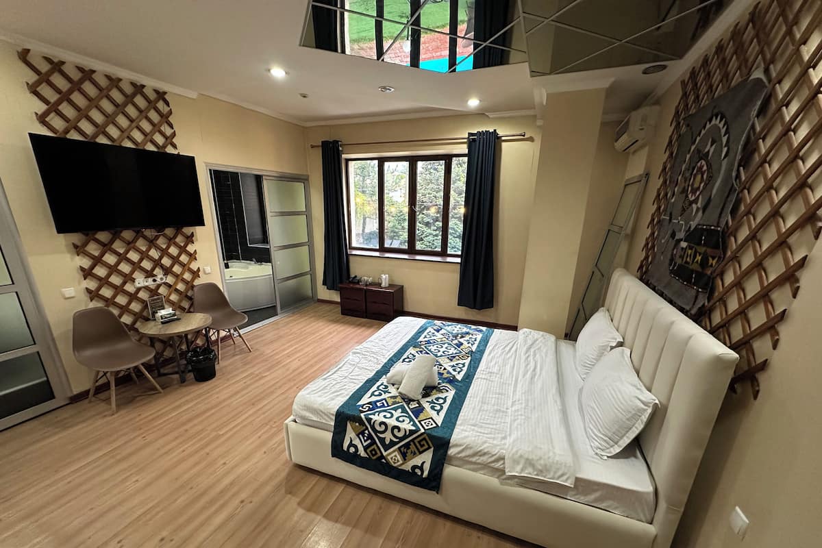 Quarto de hotel moderno com uma cama grande, uma escrivaninha, uma cadeira, uma televisão e uma janela com cortinas.