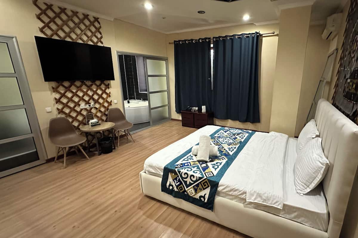 Quarto de hotel com cama, televisão, escrivaninha, cadeira, janela com cortinas e ar condicionado fixado na parede.