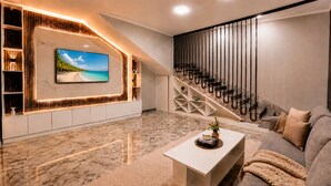 Uma sala de estar moderna com uma televisão grande, uma escada e piso de mármore.