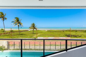 Varanda com vista para uma praia, palmeiras e um céu azul límpido.