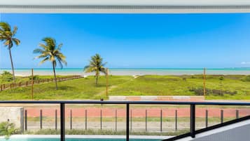 Varanda com vista para uma praia, palmeiras e um céu azul límpido.