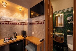 Casa de banho com lavatório, espelho, secador de cabelo e televisão fixada na parede.