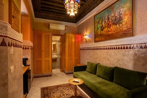 Um quarto com um sofá verde, um quadro, um candelabro e uma parede estampada.
