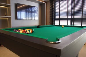 Uma mesa de bilhar com superfície de feltro verde, uma bola branca e bolas listradas.