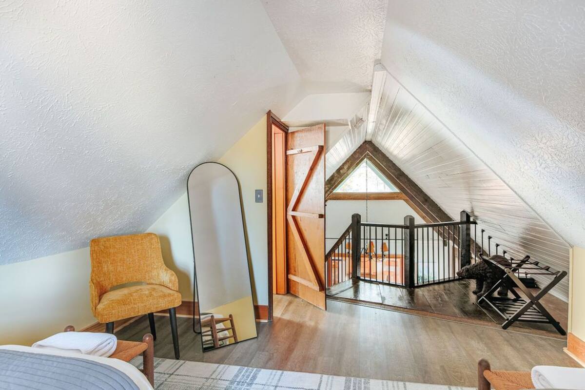 Um quarto de sótão aconchegante com teto inclinado, escada de madeira, cama de cachorro e uma cadeira.
