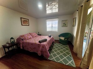 Quarto com cama, mesa de cabeceira, cadeira, janela e vista para o mar.