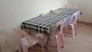 Uma área de refeições com uma mesa coberta por uma toalha quadriculada, cercada por cadeiras de plástico cor-de-rosa.