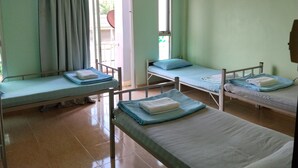 Quarto com quatro camas de solteiro, uma janela e porta que dá para o exterior.