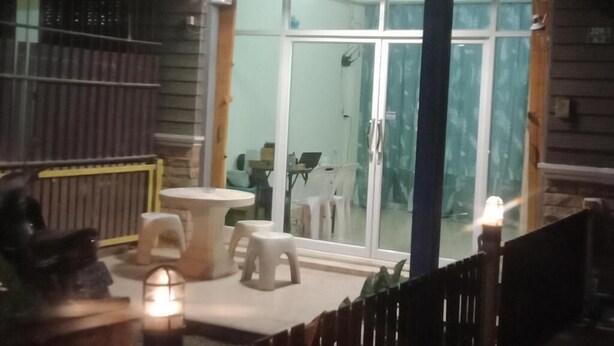 Quarto com porta de vidro para uma varanda, uma pequena mesa redonda, dois banquinhos brancos e um candeeiro.