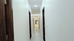 Um corredor comprido e estreito com paredes brancas e chão brilhante, que leva a uma porta no final.