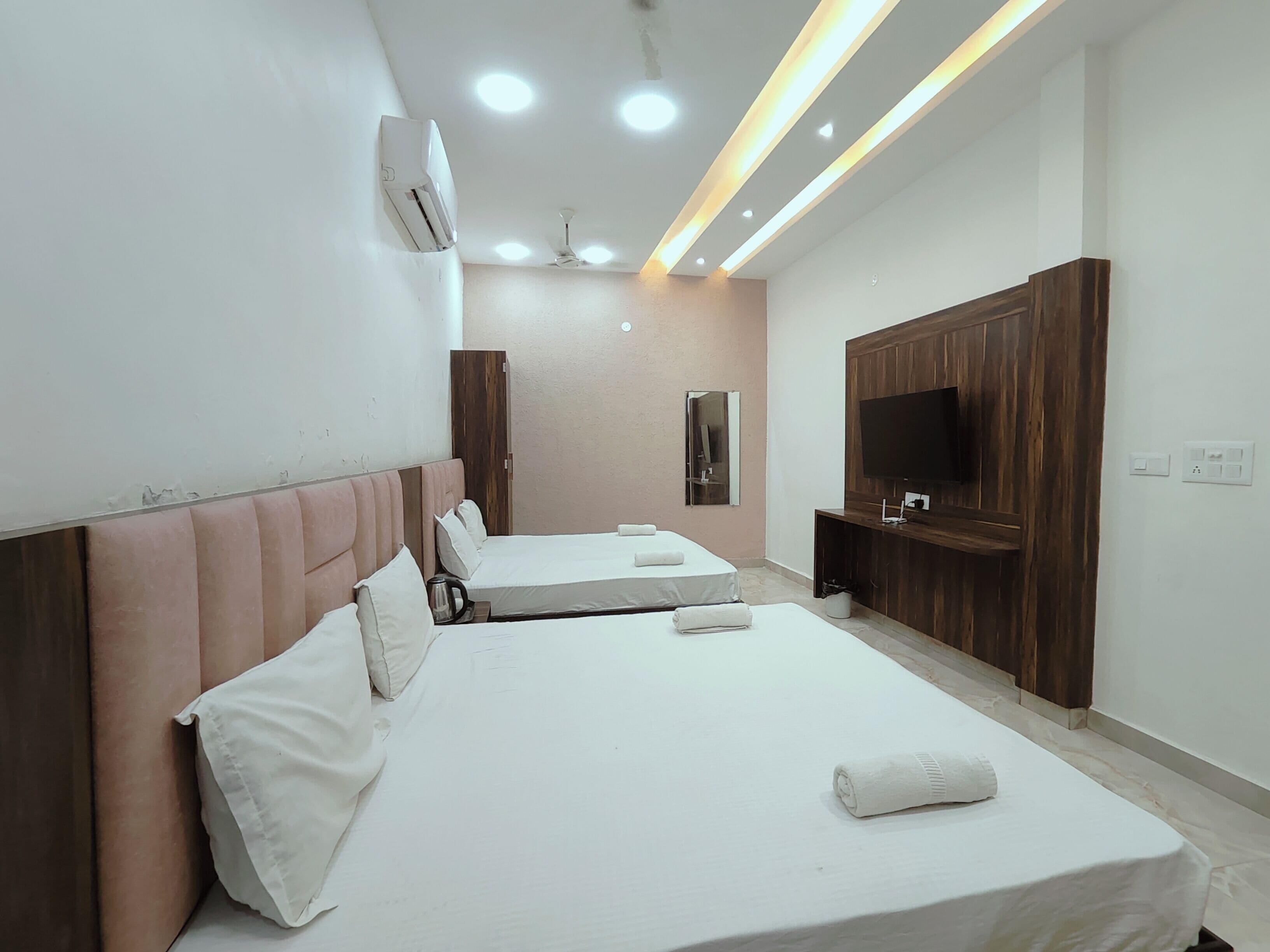 Quarto de hotel com duas camas, uma televisão, um espelho e um ventilador de teto.