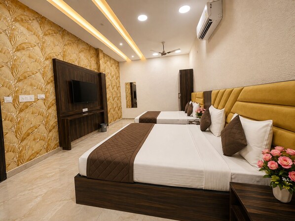 Quarto de hotel com duas camas, televisão, ventoinha no teto e ar condicionado fixado na parede.