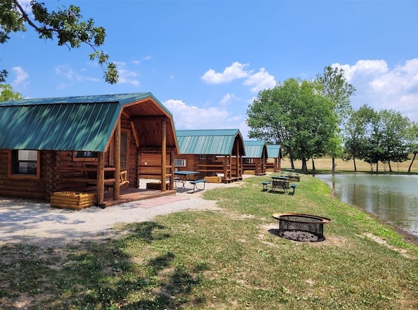 Alojamento rústico estilo cabana, com varanda coberta, mesas de piquenique e lareira.