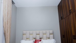 Quarto com cama, cabeceira, guarda-roupa e luminária no teto.