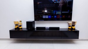 Uma sala de estar moderna com uma TV de tela plana presa à parede, um móvel preto embaixo e dois pares de chocalhos no móvel.