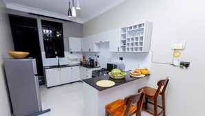 Uma cozinha moderna com armários brancos, bancada preta e cadeiras de madeira.